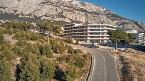 Um hotel de vários andares com design moderno, situado perto de uma área montanhosa com estrada sinuosa.