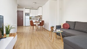 Uma sala de estar moderna com um sofá cinzento, uma pequena mesa de centro de vidro e uma área de jantar com uma mesa e cadeiras brancas.