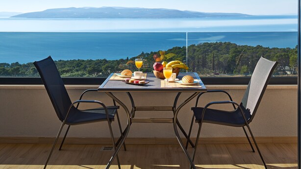 Uma mesa de jantar com cadeiras, itens de café da manhã e vista para o mar.