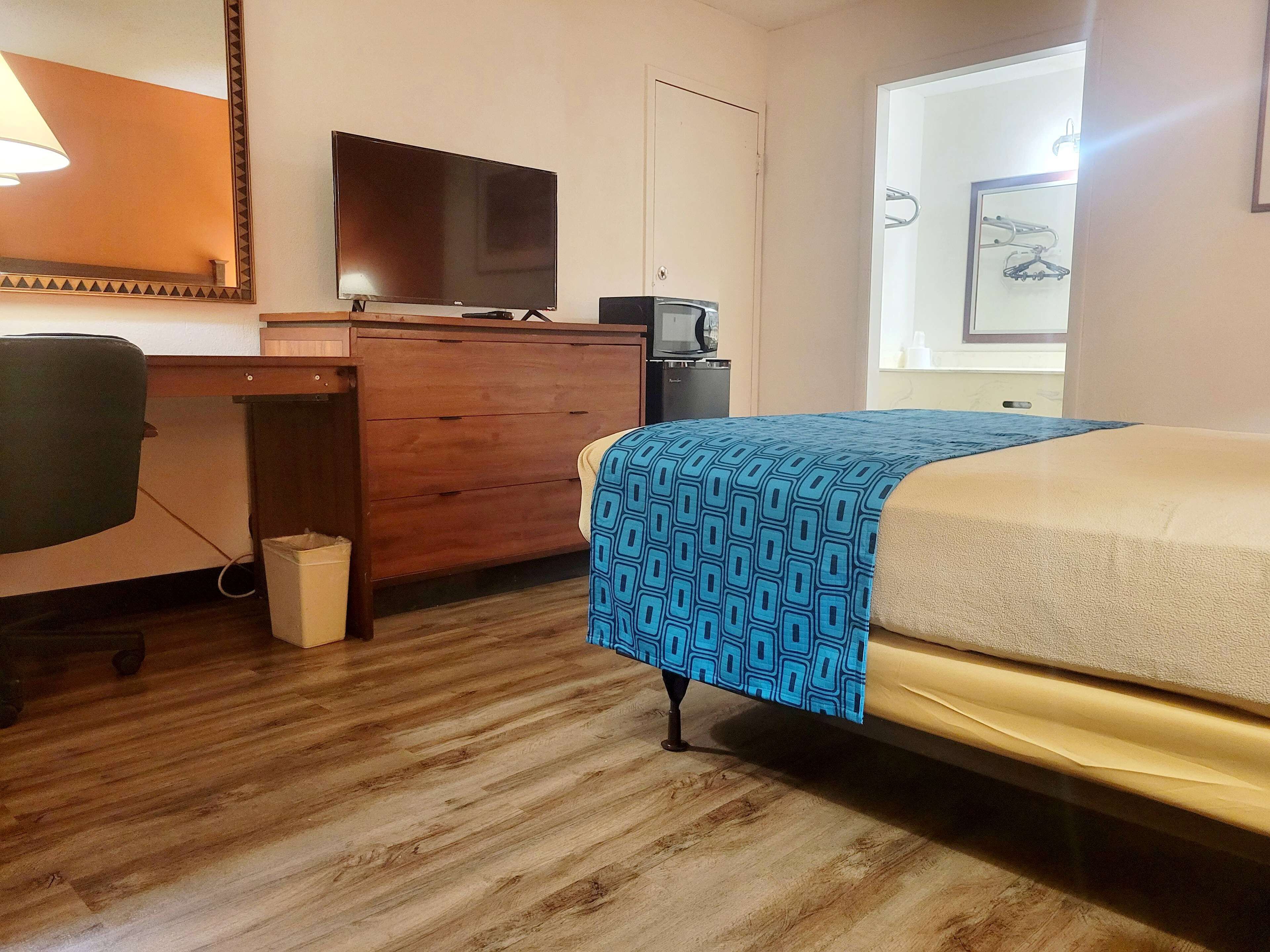 Quarto de hotel com cama, escrivaninha, televisão e guarda-roupa.