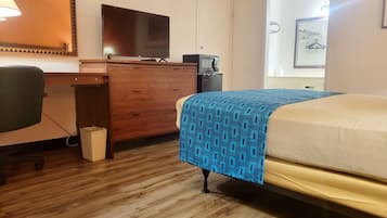 Quarto de hotel com cama, escrivaninha, televisão e guarda-roupa.