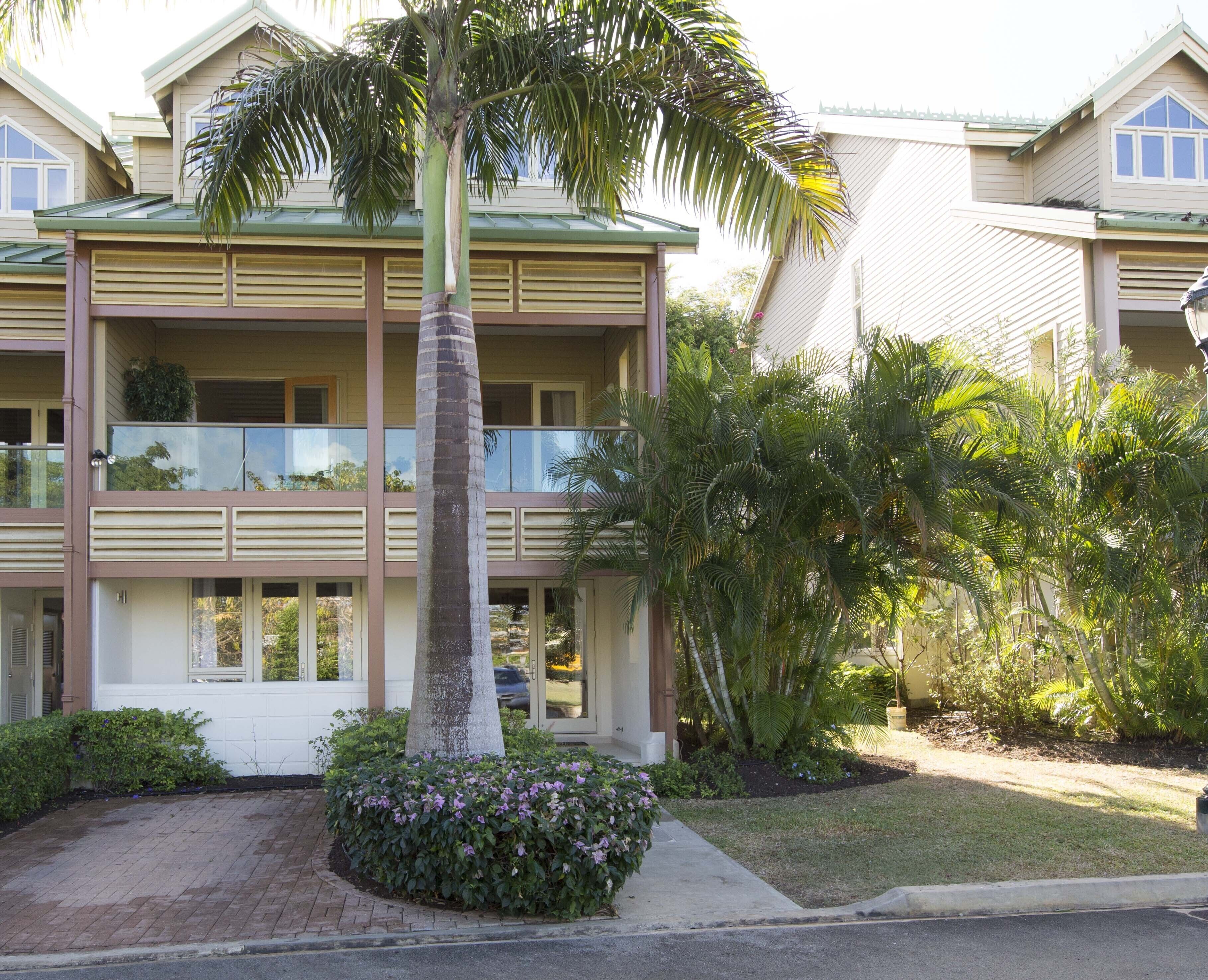 Um hotel com vários andares, varandas, palmeiras e um jardim bem cuidado.