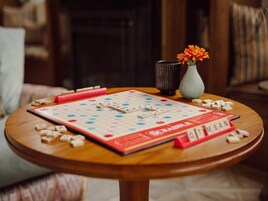 Um jogo de Scrabble sobre uma mesa de madeira, com um vaso de flores e uma xícara.