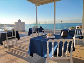 Um terraço com mesas e cadeiras, com vista para o mar.