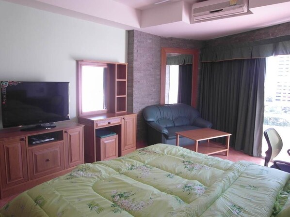 Quarto de hotel com cama, televisão, cadeira, mesinha e janela com cortinas.