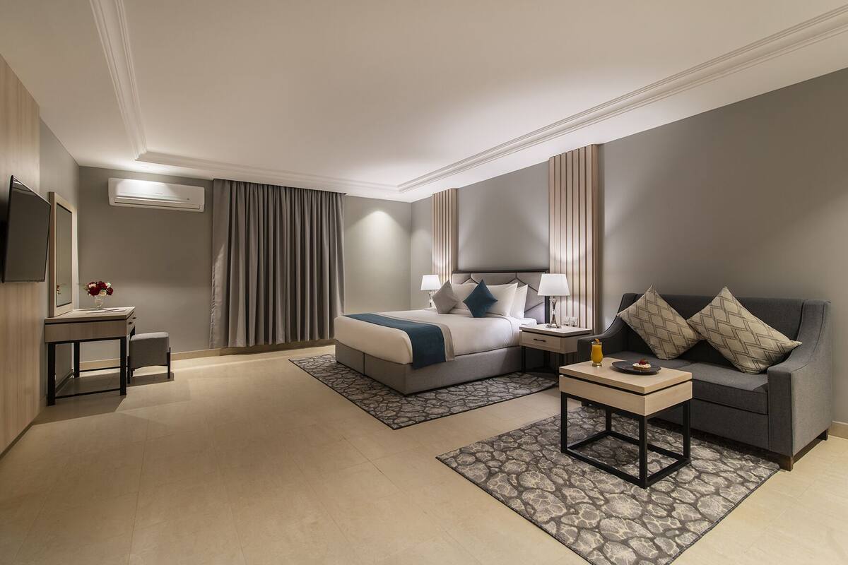 Quarto de hotel moderno com cama, mesas de cabeceira, um sofá e uma televisão.