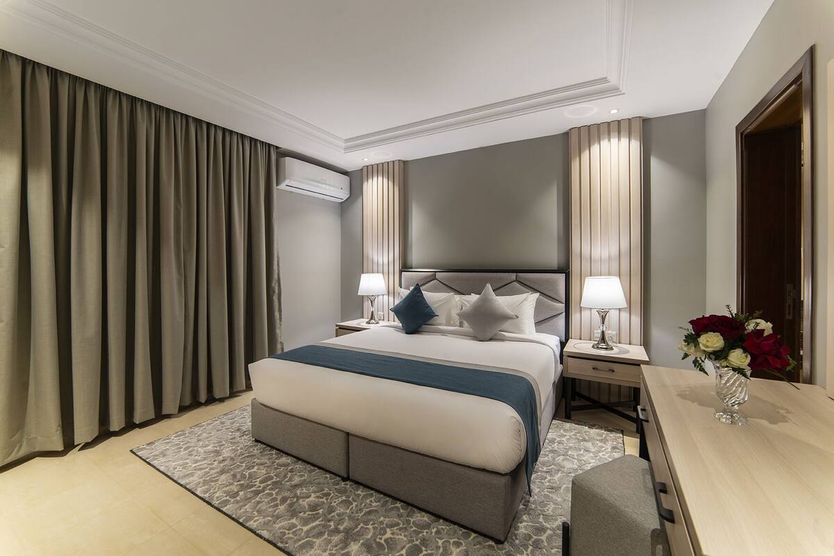Quarto de hotel moderno com uma cama grande, mesas de cabeceira, uma escrivaninha e um vaso de flores.