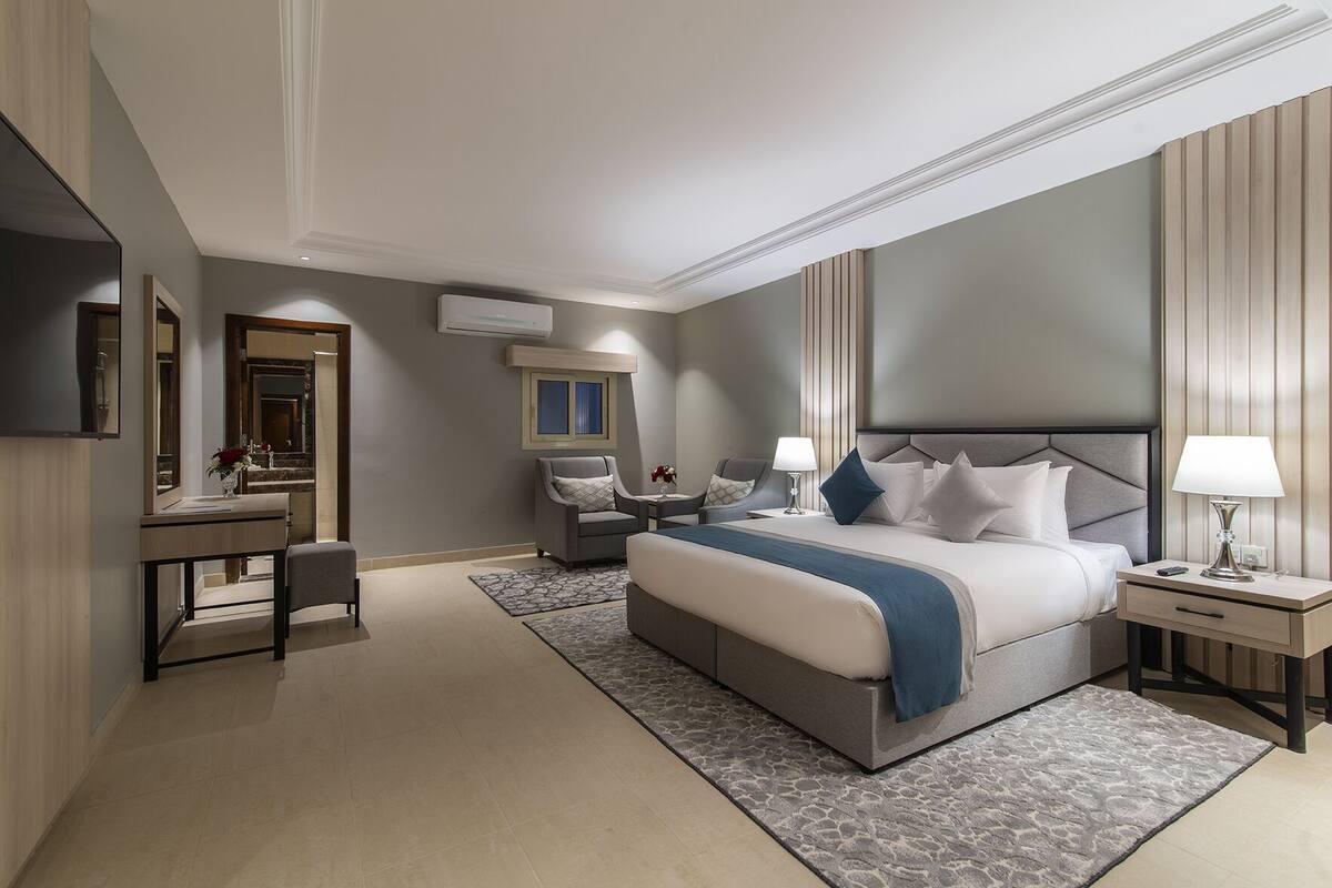 Quarto de hotel moderno com cama grande, escrivaninha, cadeira e televisão.