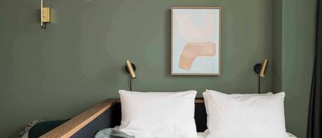Uma cama com travesseiros brancos, um cobertor verde e uma luminária moderna.