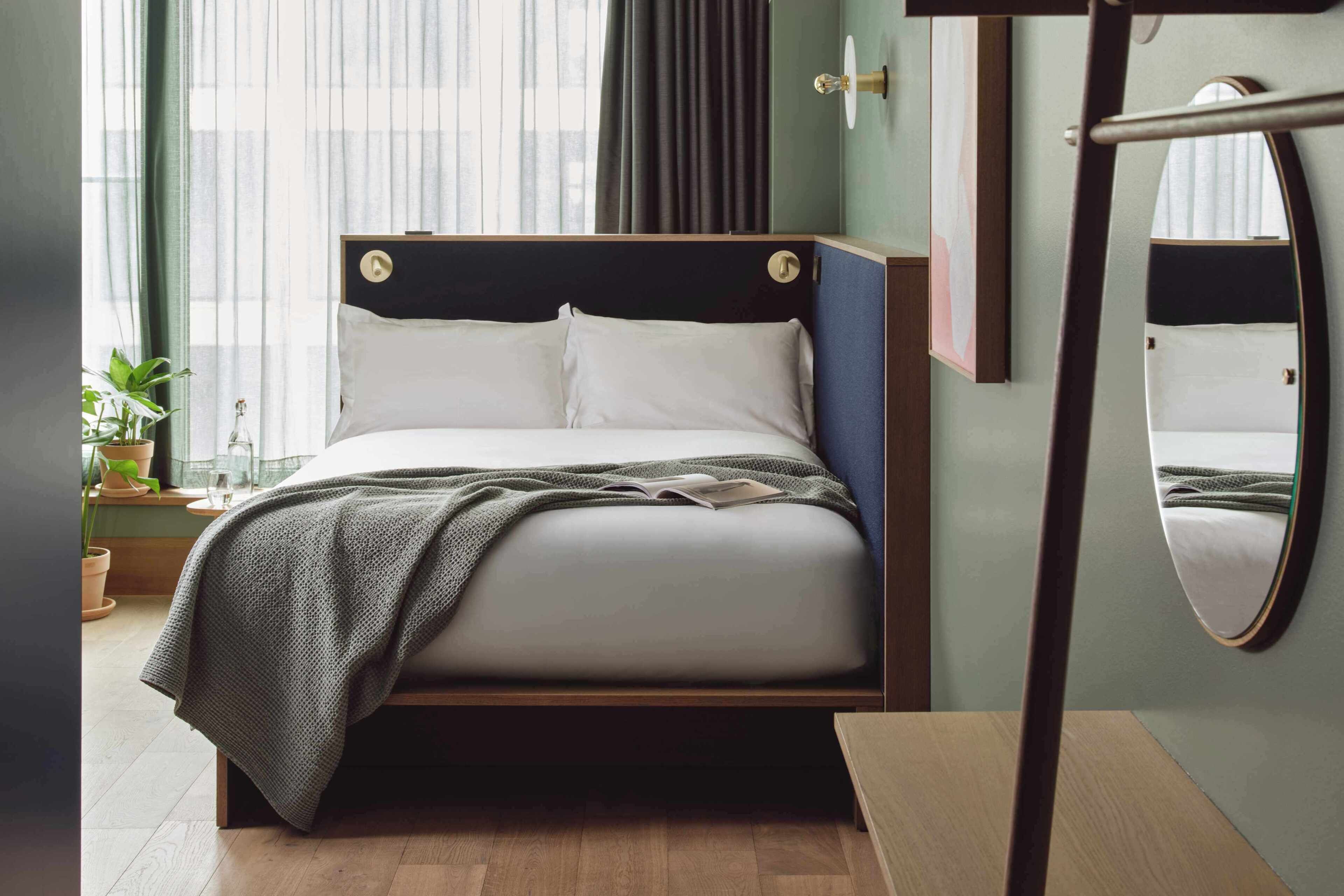 Um quarto moderno com uma cama, uma janela com cortinas, um vaso de planta e um espelho.