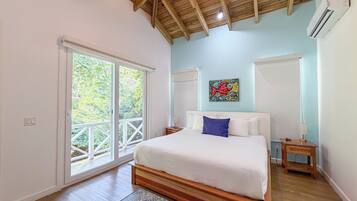 Quarto com teto de madeira, uma cama grande, mesa de cabeceira e janela com vista para o verde.