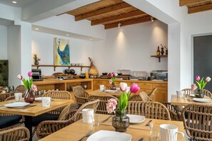 Uma sala de jantar com mobiliário de vime, pratos brancos e vasos com flores.