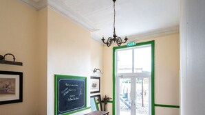 Uma área de recepção com um balcão de madeira, uma lousa com escrita, uma porta com moldura verde e uma escadaria que dá para o exterior.