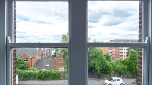 Janela com vista para uma rua residencial, casas e um carro estacionado.