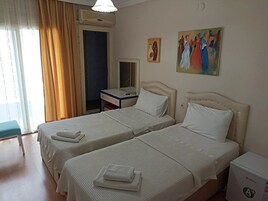 Quarto de hotel com duas camas, uma escrivaninha, uma cadeira, um aquecedor e um quadro na parede.
