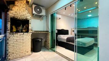 Quarto com lareira de tijolos, uma cama, porta de vidro que dá para uma varanda e ar-condicionado Samsung.