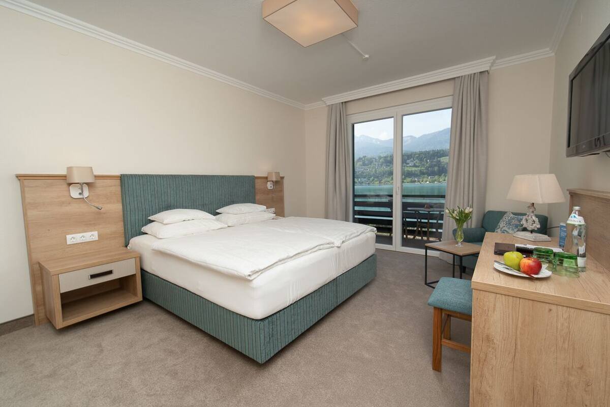 Quarto de hotel com cama, mesa de cabeceira, escrivaninha e vista para uma varanda.