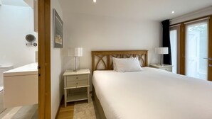 Quarto com cama grande, cabeceira de madeira, mesas de cabeceira com luminárias, pequena gaveta ao lado da cama e espelho na parede.