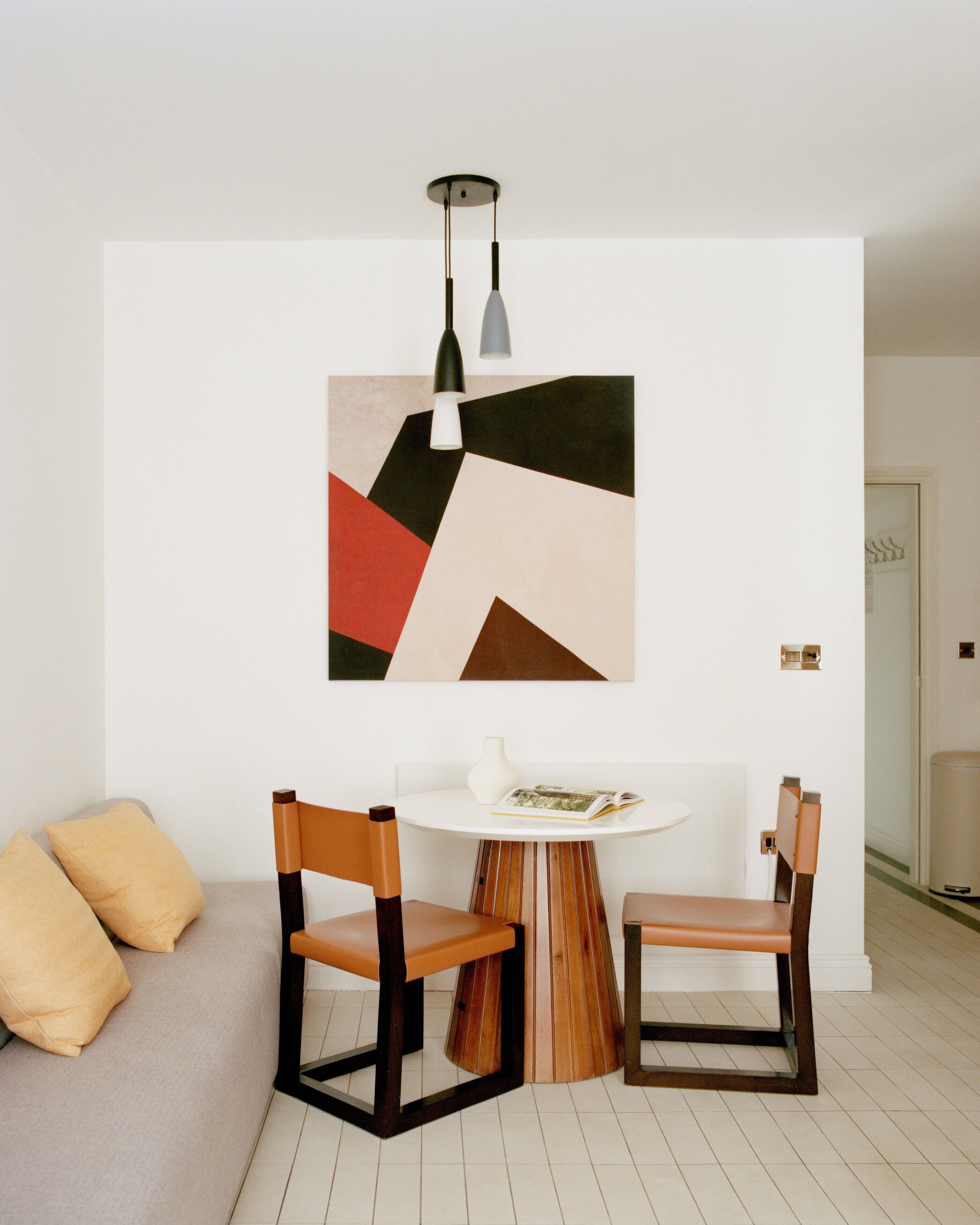 Uma sala de jantar com uma mesa redonda, duas cadeiras e uma luminária fixada na parede.