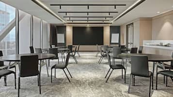 Uma sala de conferências moderna com mesas e cadeiras redondas, uma tela grande e vista para a cidade.