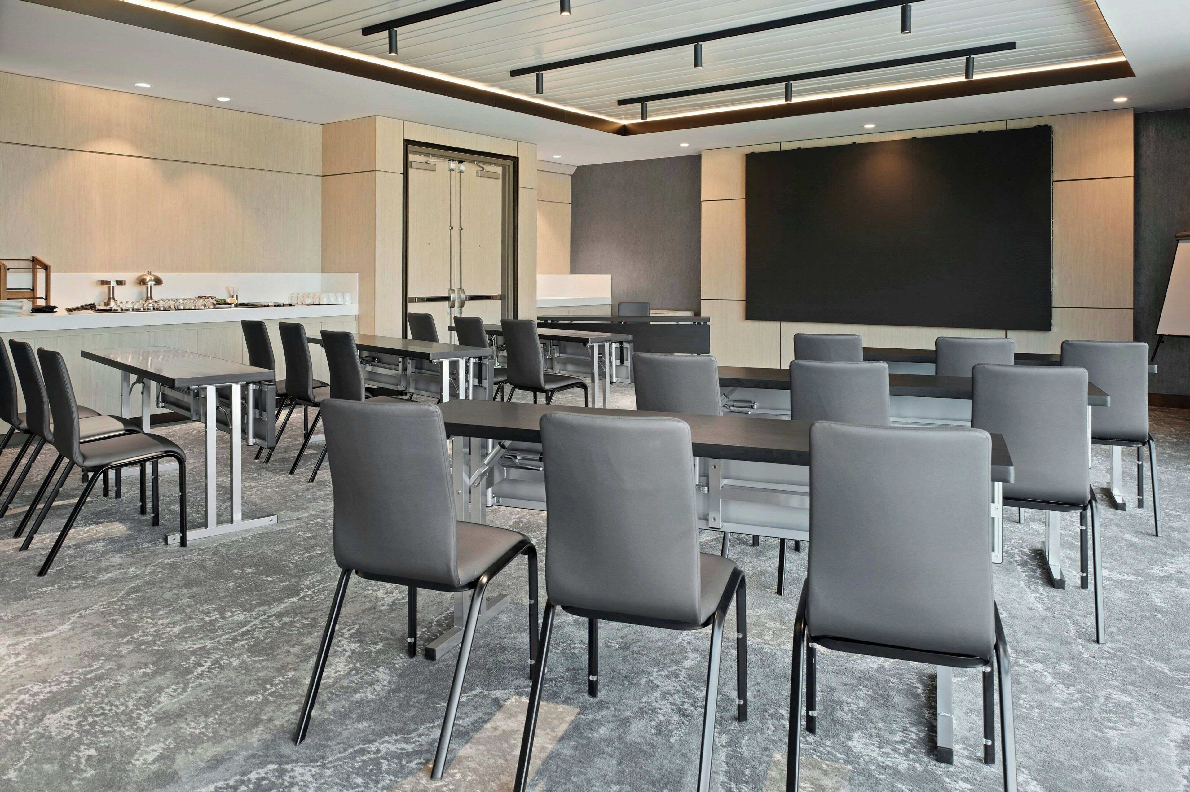 Uma sala de conferências moderna com uma mesa grande, várias cadeiras, uma tela de projetor e uma tela de apresentação.