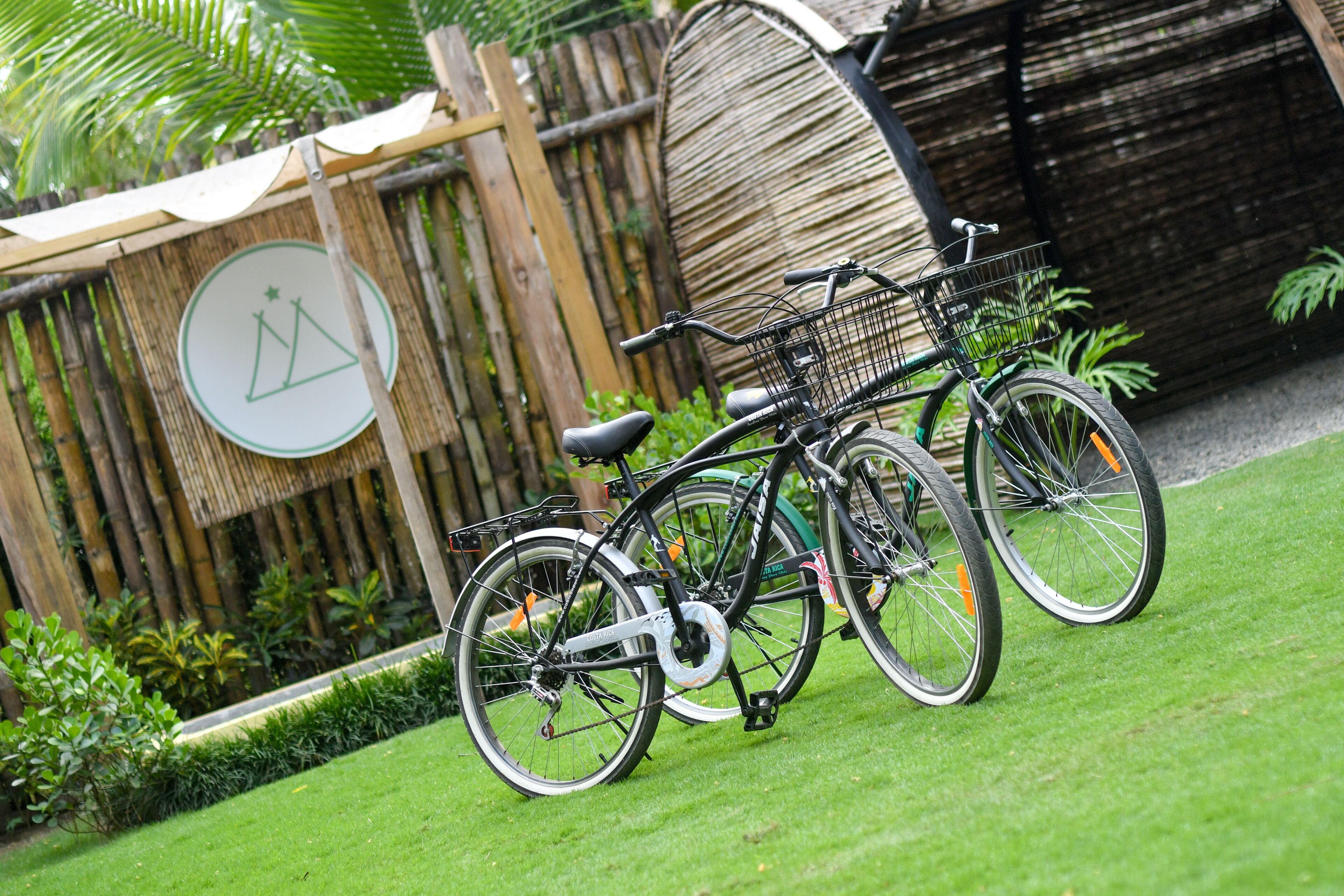 Uma bicicleta estacionada em um gramado bem cuidado, com uma cerca de madeira e um letreiro circular ao fundo.
