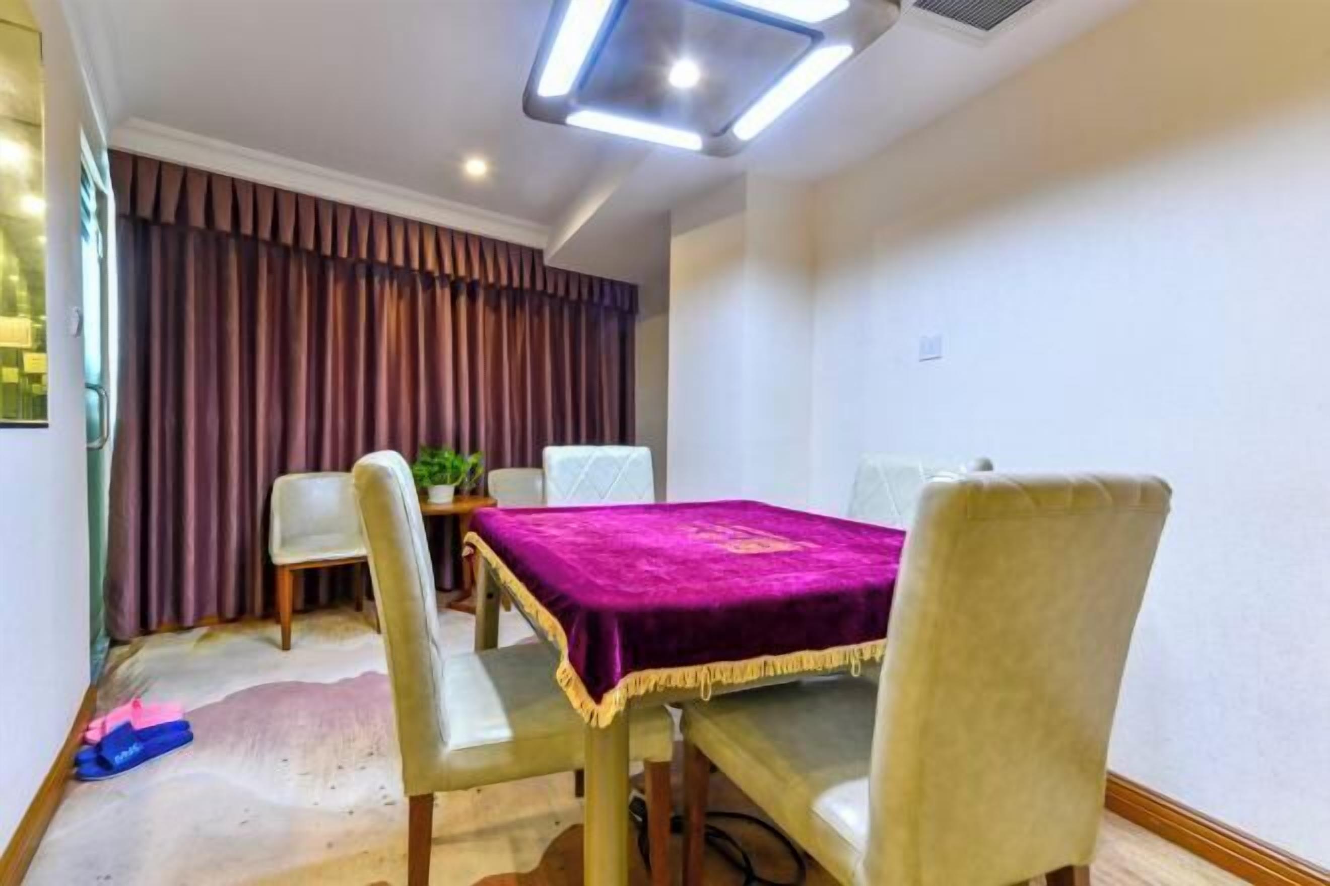 Uma sala de jantar com uma mesa coberta por um tecido roxo, quatro cadeiras e um lustre.