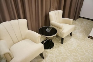 Quarto com duas poltronas cor de creme e uma pequena mesa preta com um copo.