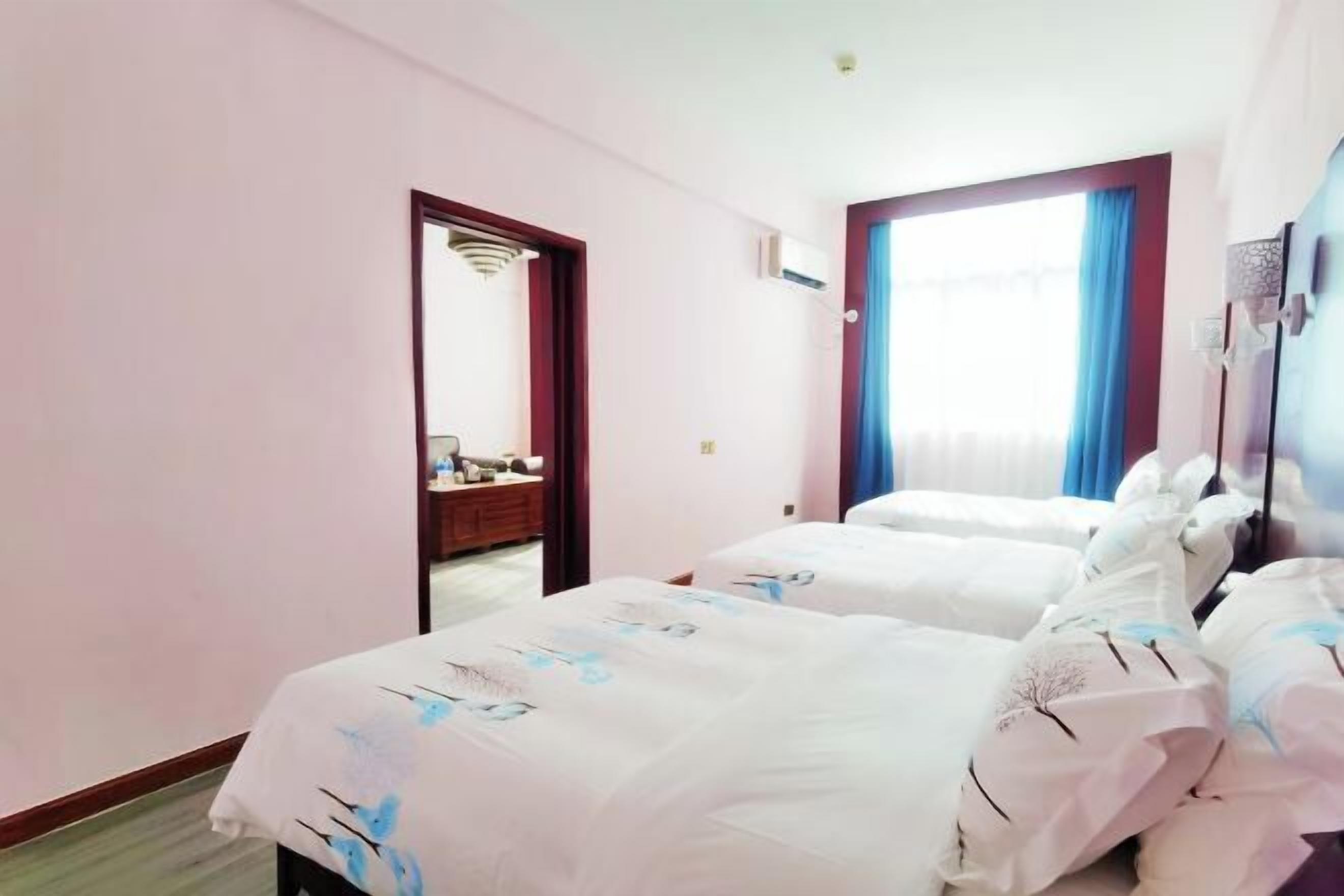 Quarto de hotel com duas camas, um espelho, uma porta e uma janela com cortinas.
