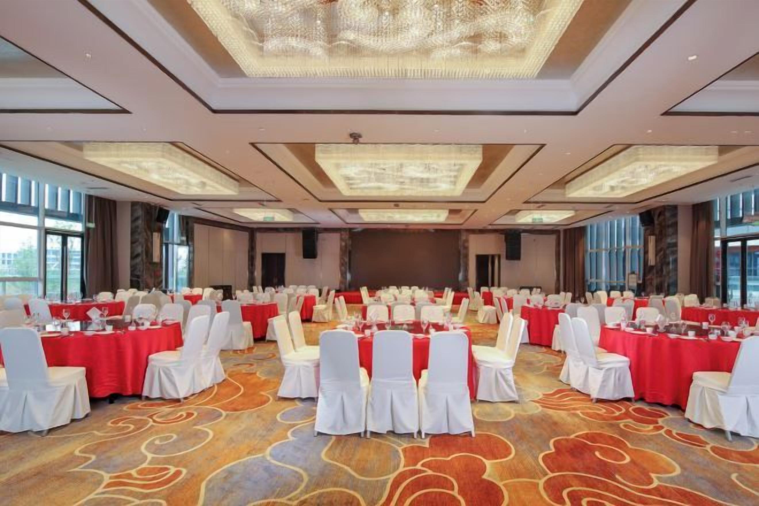 Uma sala de banquetes com mesas redondas, cadeiras brancas e toalhas de mesa vermelhas.