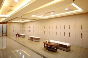 Um saguão de hotel com uma longa fileira de armários, uma área de estar com uma mesa redonda e um banco.