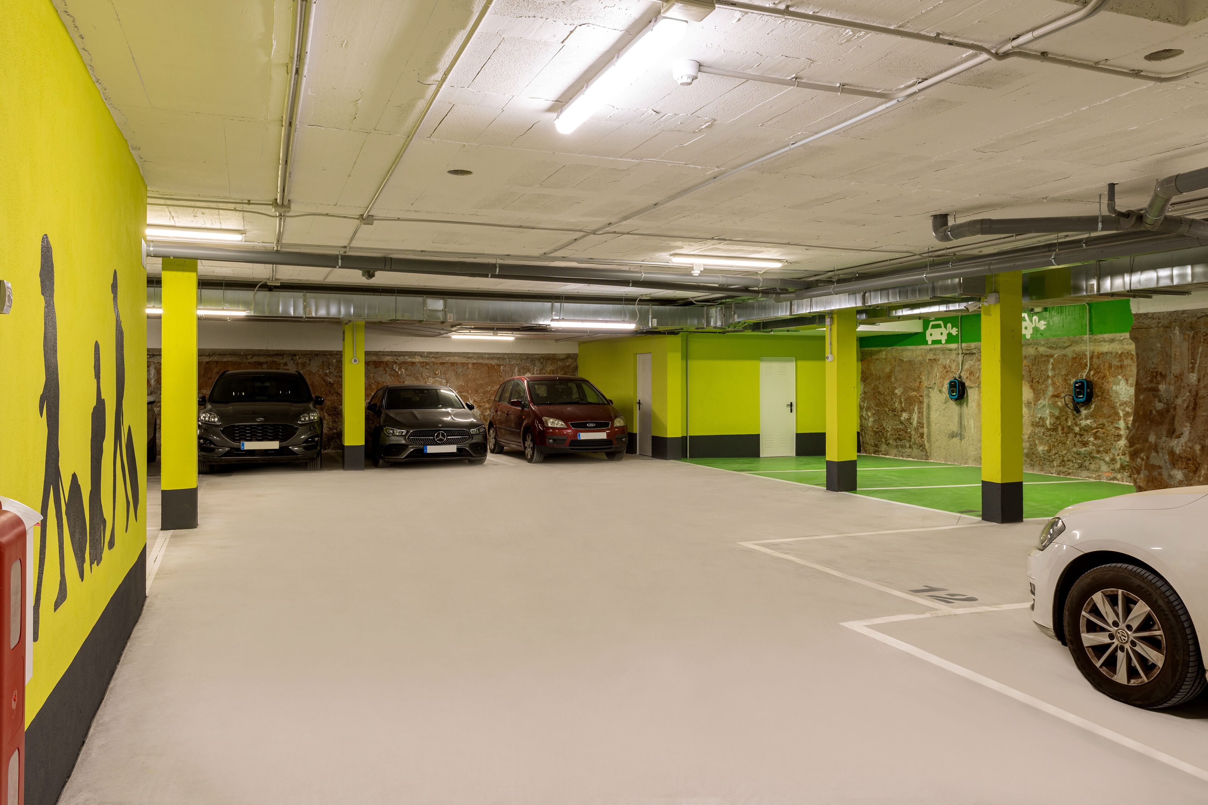 Um estacionamento multi andar com pilares amarelos e verdes, diversas vagas e um carro branco estacionado em uma delas.