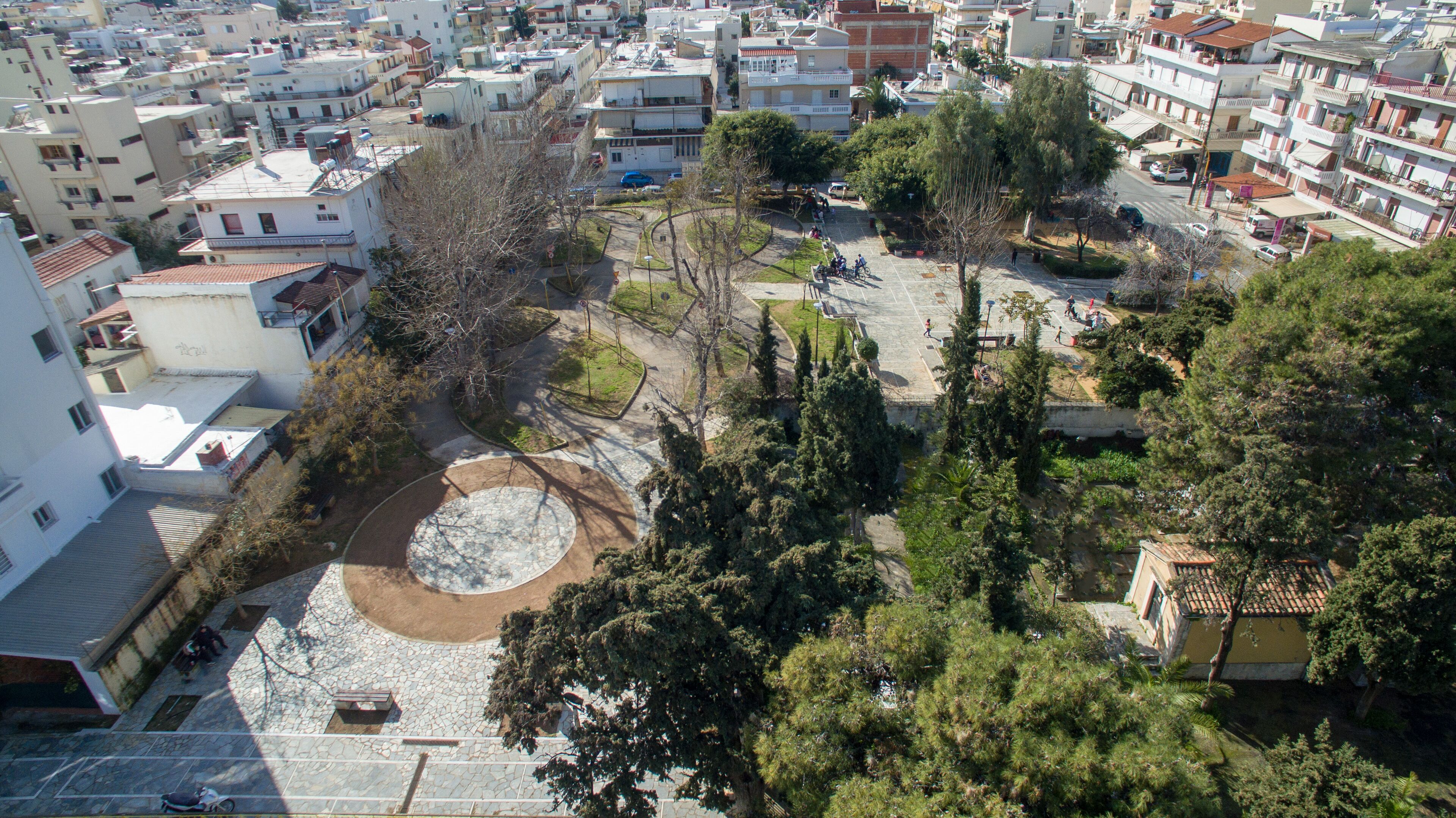 Vista aérea de uma área residencial com vários edifícios, uma praça circular central e áreas verdes ao redor.
