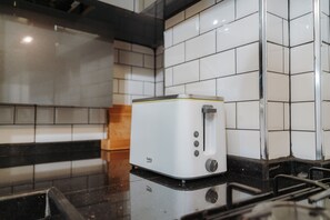 Uma cozinha com paredes azulejadas brancas, uma torradeira branca e uma bancada preta.
