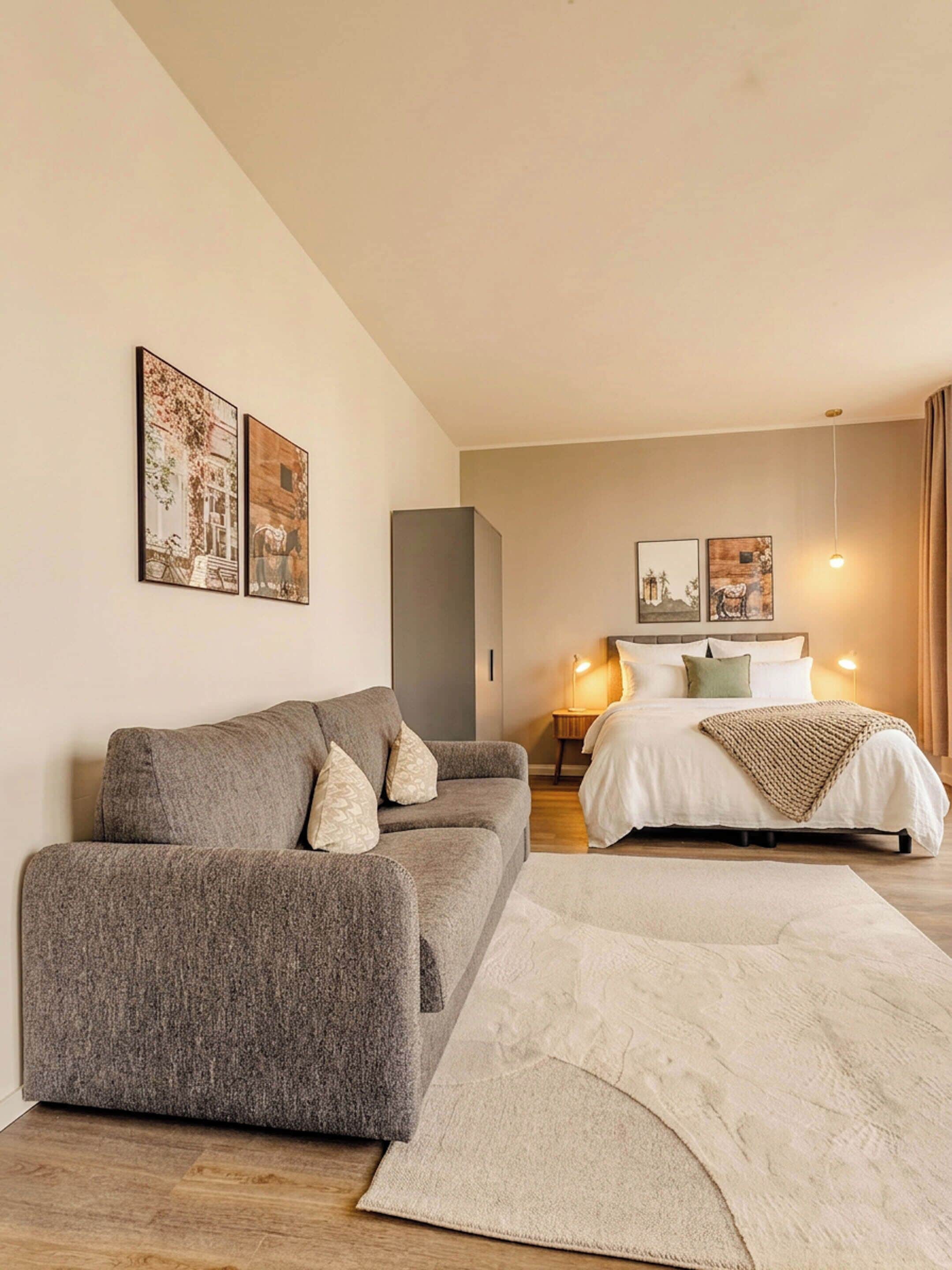 Quarto moderno com um sofá cinzento, uma cama com roupa de cama branca e duas molduras na parede.