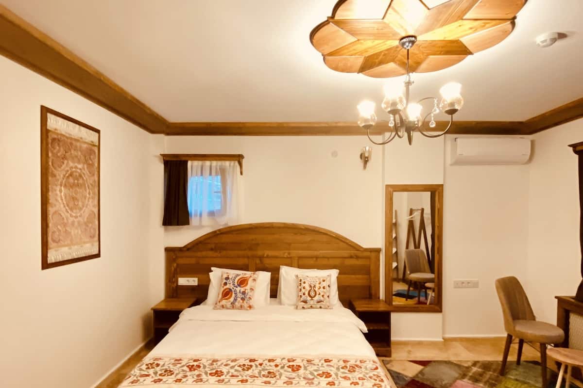 Quarto com cama de madeira, um candelabro, um espelho, uma cadeira e um tapete colorido.