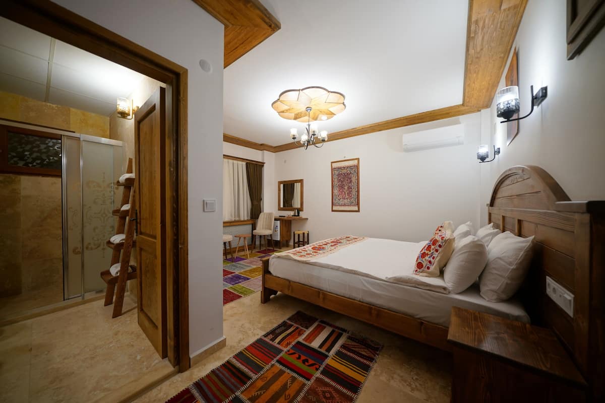 Quarto com cama de madeira, tapete estampado, lustre e banheiro com chuveiro e porta-toalhas.