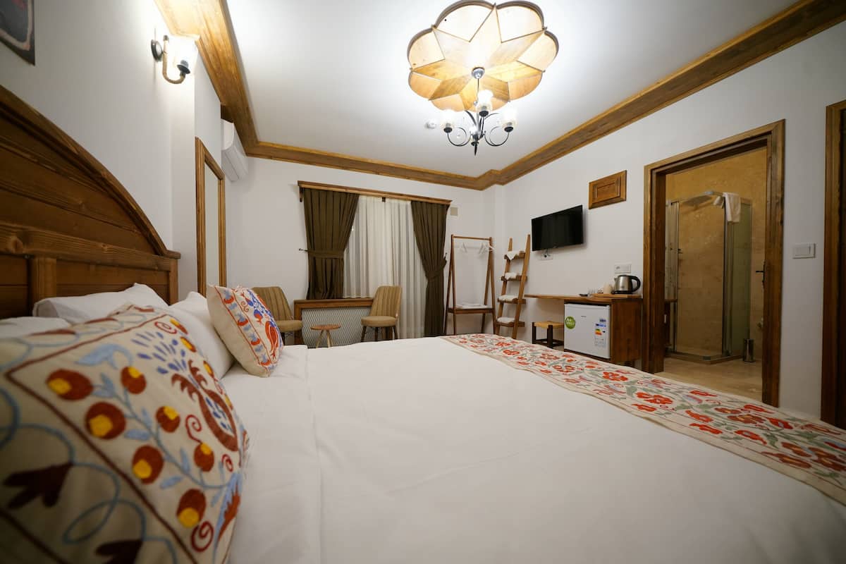 Quarto de hotel com uma cama grande, uma escrivaninha, uma cadeira, uma televisão e um chuveiro.