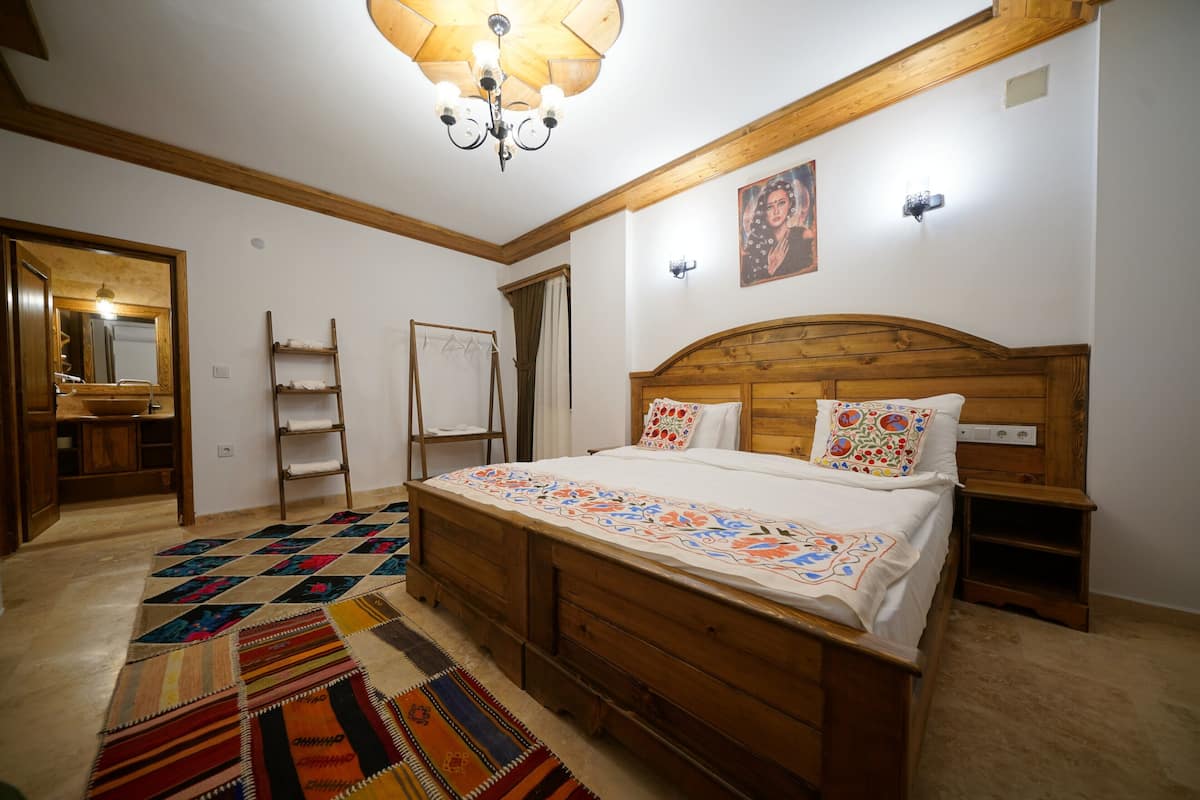 Quarto com cama de madeira, um candelabro, um espelho grande e um tapete colorido.