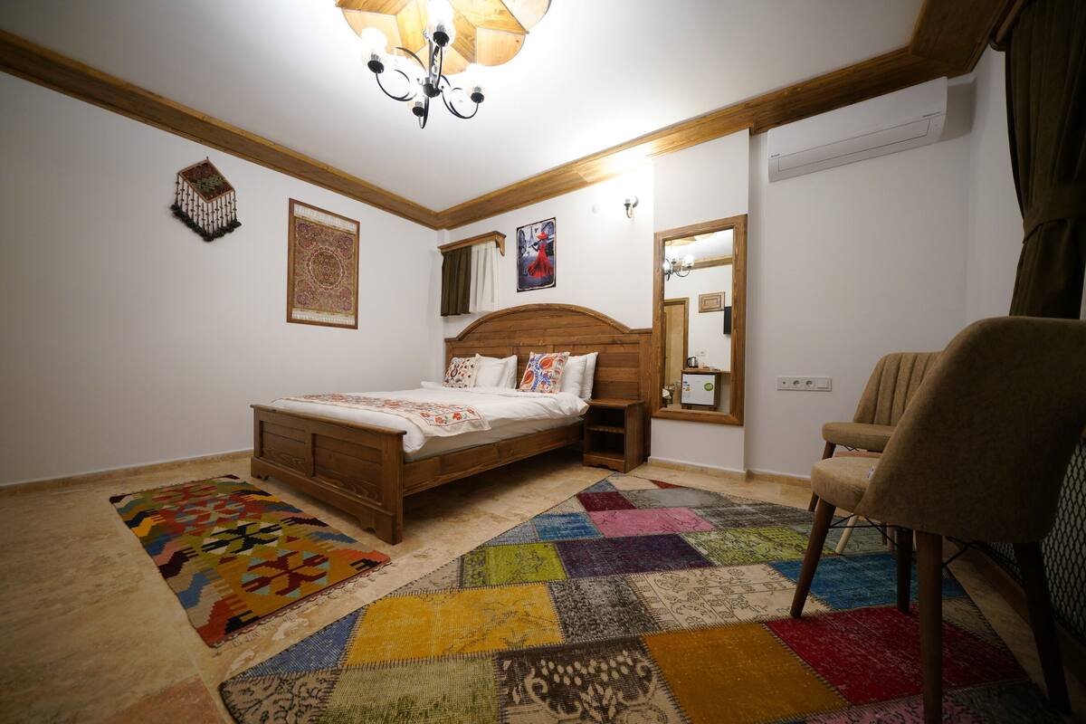 Quarto com cama de madeira, tapete de colcha colorida, cadeira de madeira e um candelabro.
