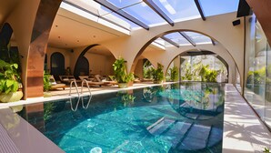 Piscina interior moderna com água azul cristalina, rodeada por áreas de descanso com assentos e plantas em vasos.