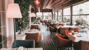 Um restaurante com mesas postas para refeições, uma escadaria e janelas amplas.