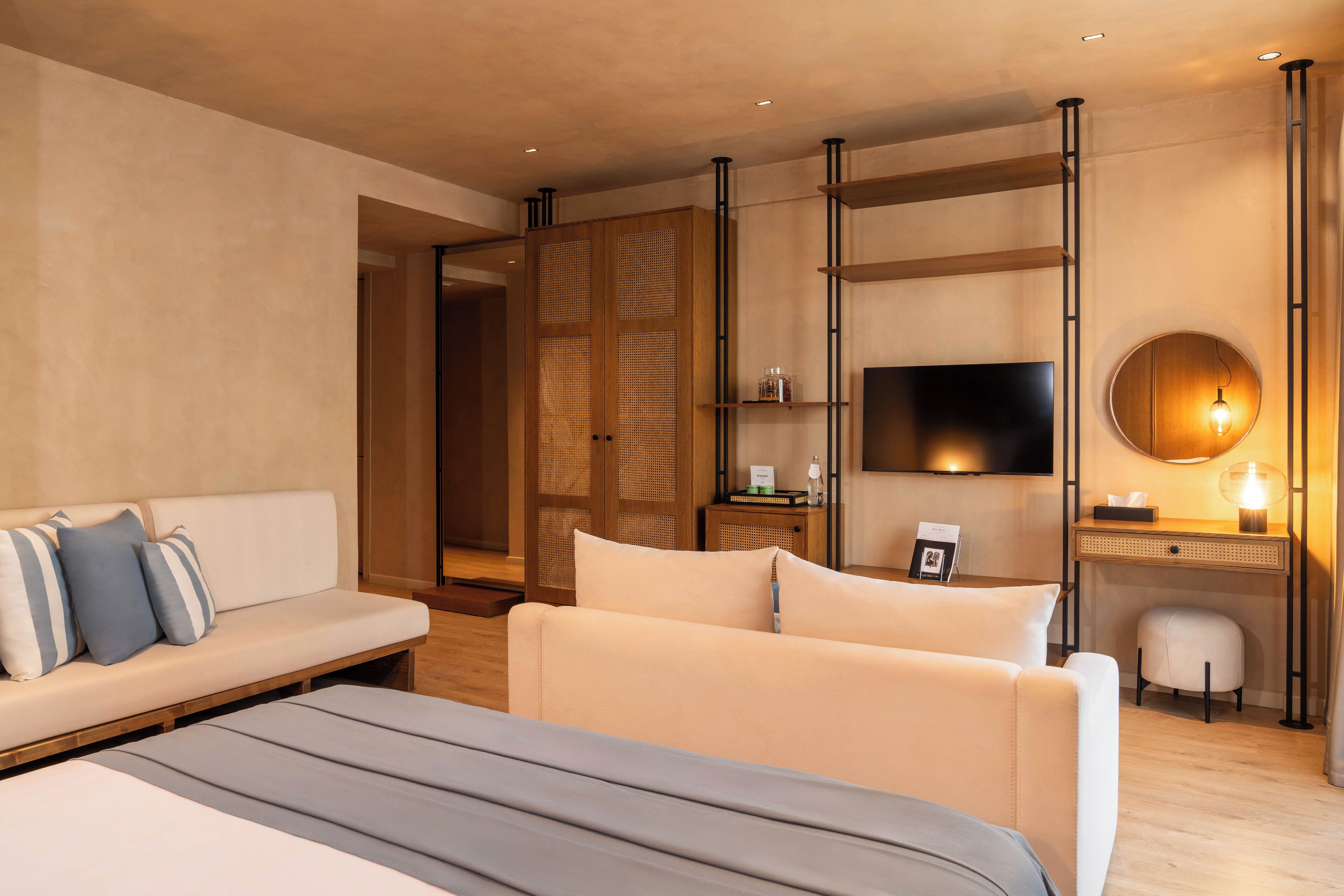 Quarto de hotel moderno com sofá, cama, televisão, escrivaninha com luminária e armário.