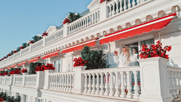 Um edifício branco com varandas decoradas com flores vermelhas e grades brancas.