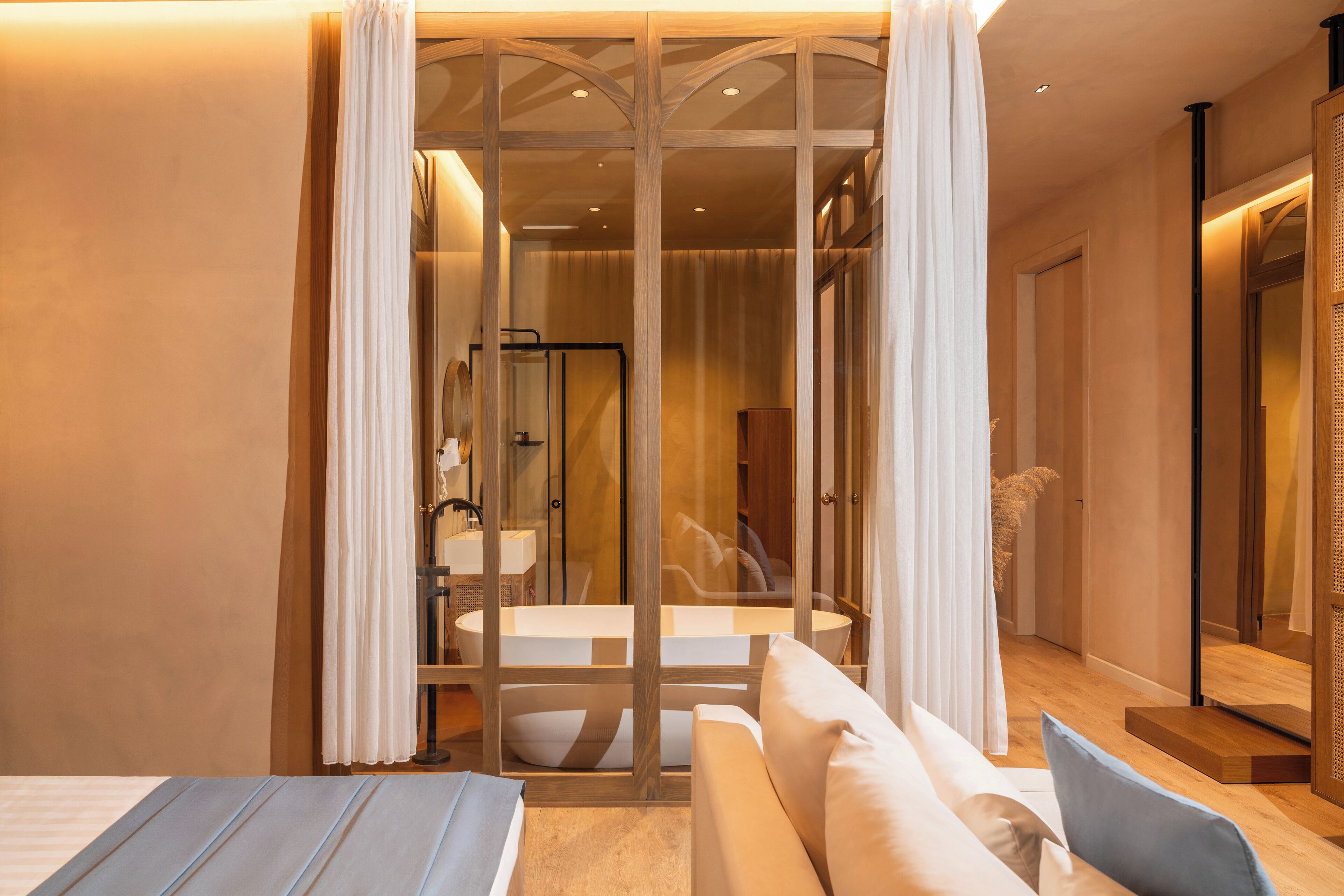 Quarto de hotel moderno com cama, sof á, divisória de vidro e banheiro visível através da divisória.