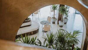 Um pátio interno com uma mesa redonda e cadeiras, cercado por plantas em vasos e um arco grande.