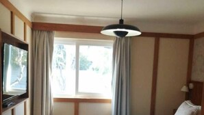Quarto com cama, televisão na parede, janela com cortinas e luminária no teto.