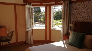 Um quarto com uma cama, duas janelas com cortinas, uma cadeira e um abajur.