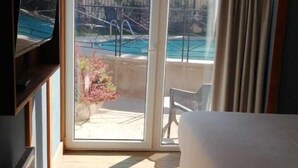 Quarto de hotel com cama, televisão e vista para piscina e área externa.
