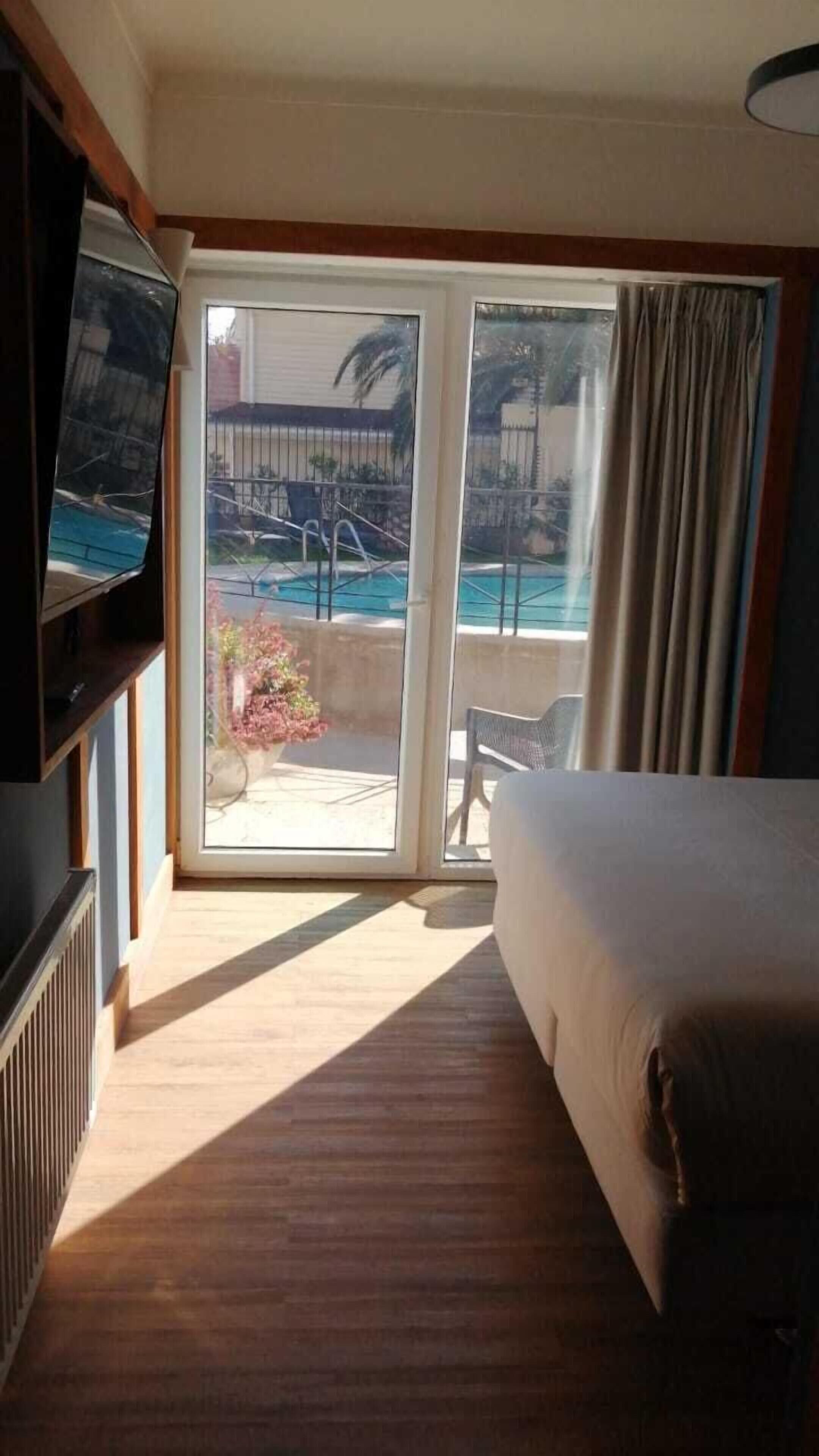 Quarto de hotel com cama, televisão, porta de vidro para área da piscina e uma cadeira.